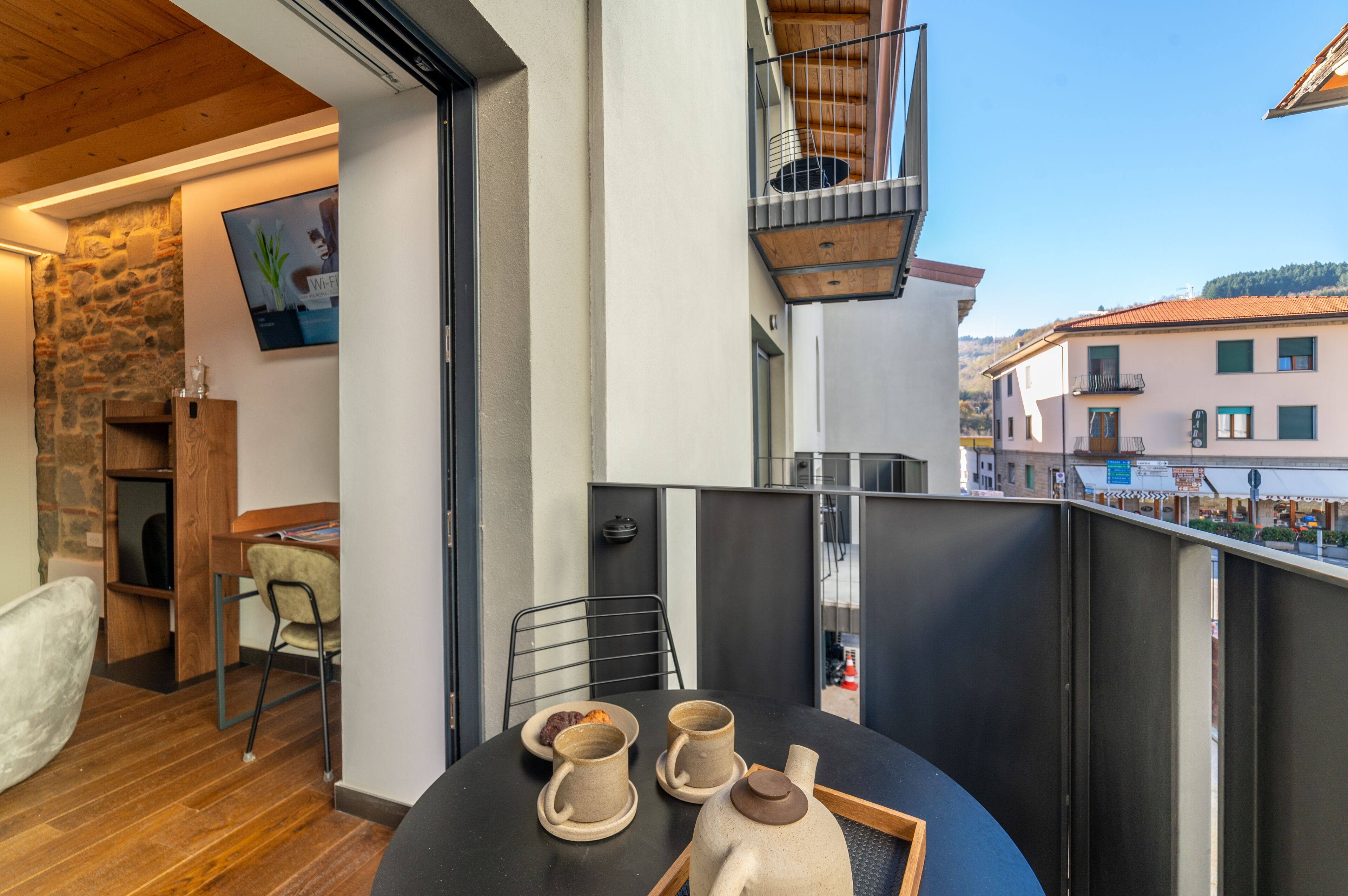 Uma varanda com uma mesa posta para chá, uma cadeira e vista para a paisagem urbana.