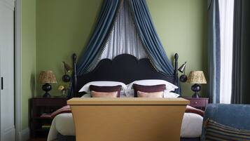 Quarto com cama, mesas de cabeceira, uma cadeira, um candelabro e janela com cortinas.