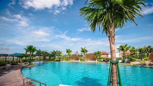 Piscina com deck de madeira, palmeiras e guarda-sóis.