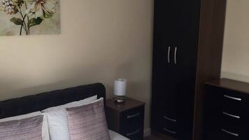 Um quarto com cama, mesa de cabeceira, guarda-roupa e luminária pendente.