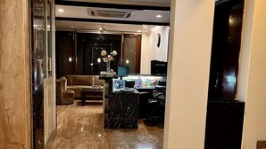 Um hall de hotel moderno com piso de mármore, balcão de recepção e área de estar com sofá e poltronas.
