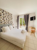 Quarto de hotel com uma cama grande, uma escrivaninha, uma cadeira, televisão de tela plana e vista para o exterior.