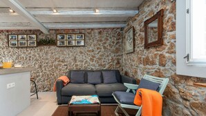 Uma sala de estar acolhedora com parede de pedra, um sofá cinza, uma mesa de centro de madeira e uma poltrona azul-claro com manta laranja.