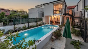 Uma casa moderna com piscina, um alpendre coberto e uma escadaria que leva a um andar superior.