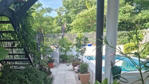 Caminho no jardim que leva a uma área de piscina, com plantas em vasos e um cercado de madeira.
