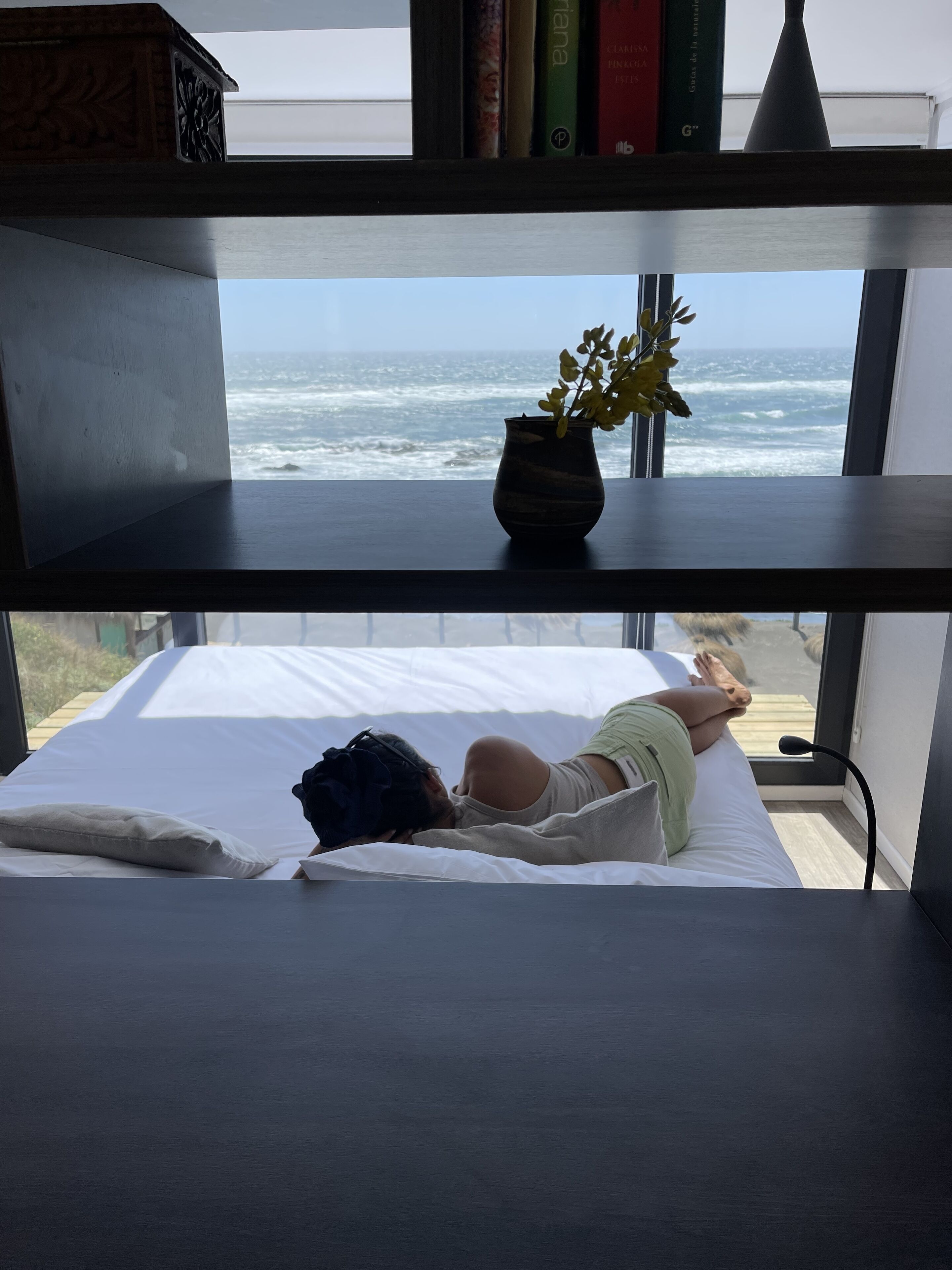 Um quarto com uma cama, uma estante de livros e vista para o oceano.