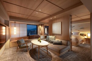 Quarto de hotel moderno com teto de madeira, uma janela ampla com vista para a cidade, sofá, mesa pequena e cama.