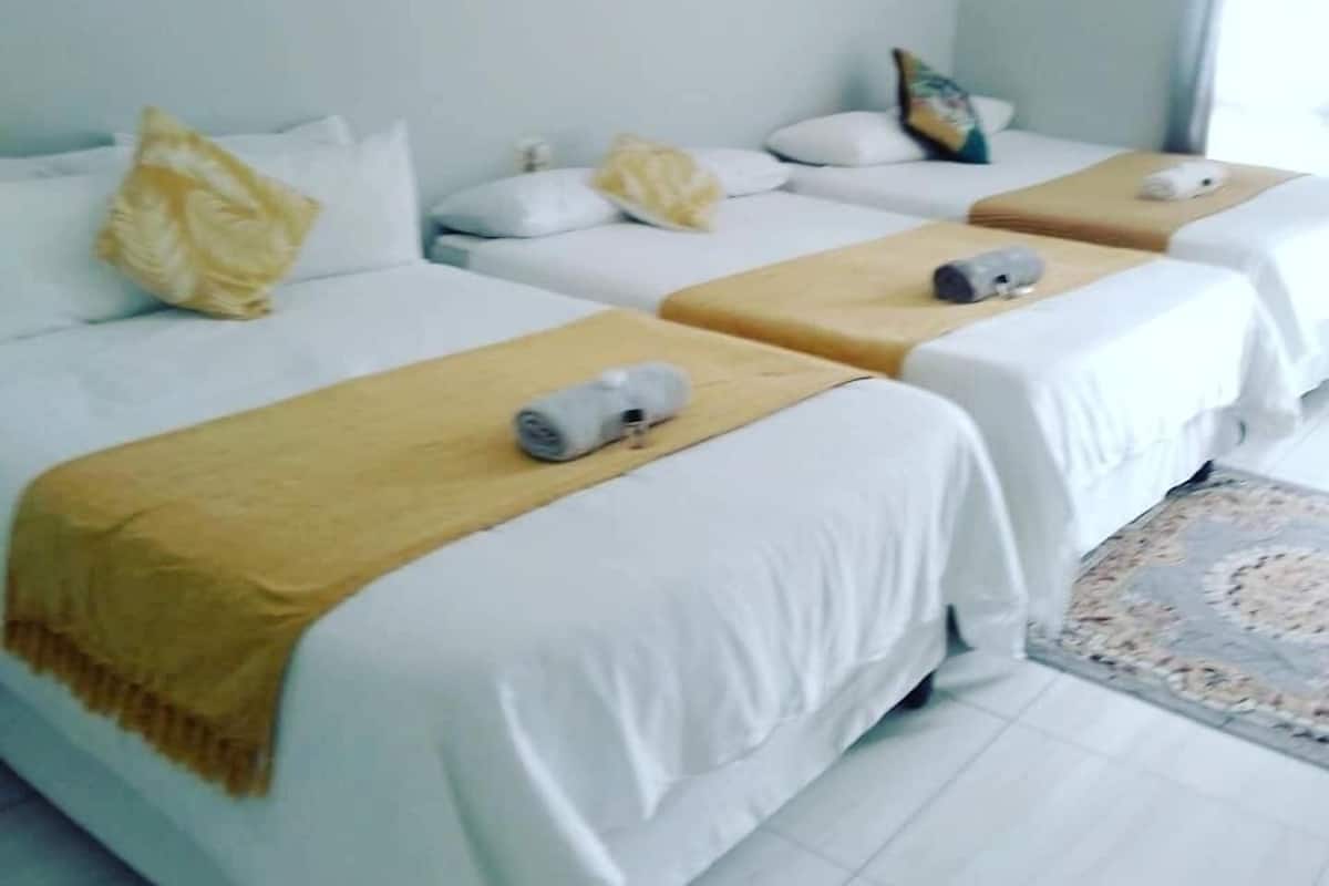 Quarto de hotel com duas camas, roupa de cama branca, mantas amarelas e um tapete estampado.