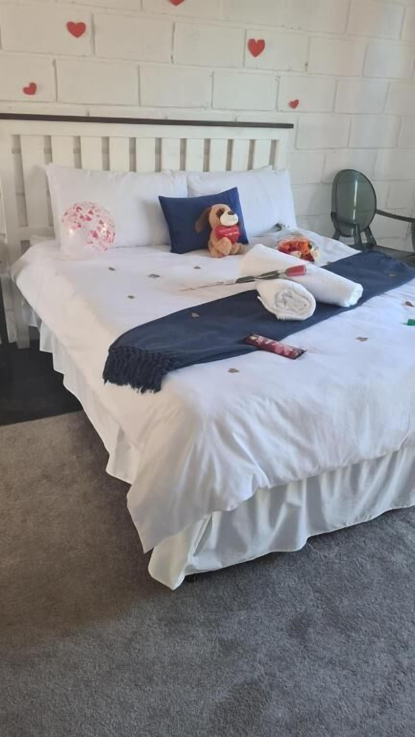 Cama bem arrumada com um cobertor azul, um urso de pelúcia e um travesseiro com estampa de coração.