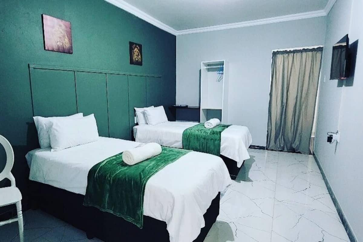 Quarto de hotel com duas camas, uma cadeira, um guarda-roupa e um espelho.