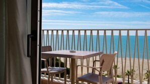 Uma varanda com mesa e cadeiras, com vista para uma praia e um céu claro.