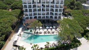 Hotel com vários andares e piscina no terraço, rodeado por áreas de estar ao ar livre e guarda-sóis.