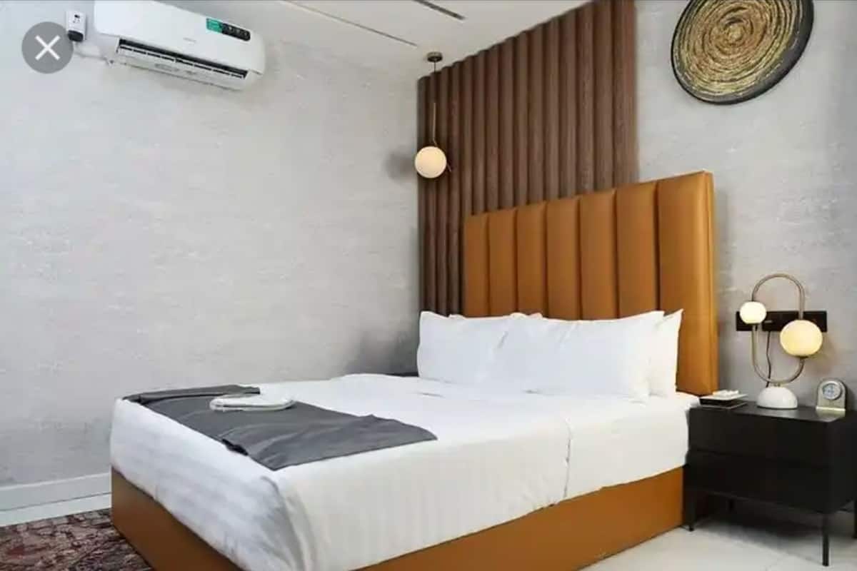 Um quarto moderno com cama, mesa de cabeceira, abajur e ar condicionado fixado na parede.