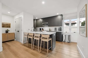 Uma cozinha moderna com uma ilha central, banquetas e um micro-ondas.