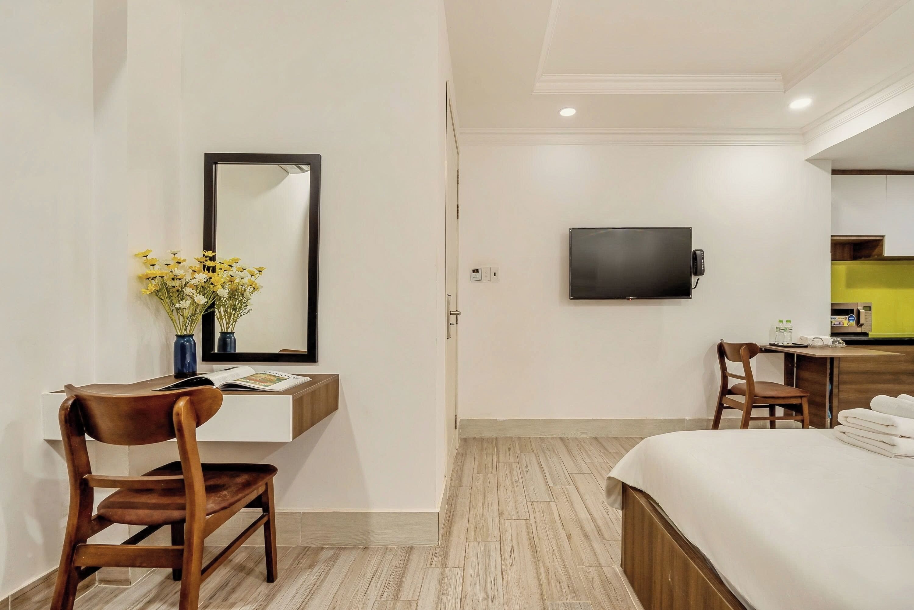 Quarto de hotel com cama, escrivaninha, cadeira, televisão e espelho.