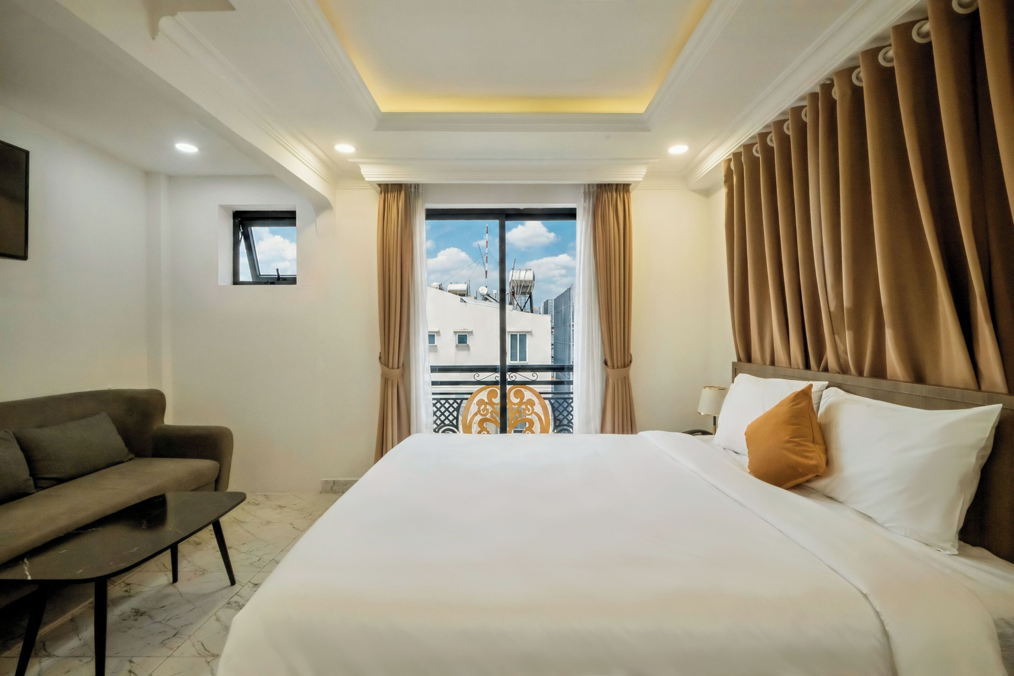 Quarto de hotel com cama, sofá, janela com cortinas e vista para edifícios.