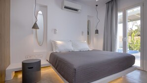 Quarto moderno com uma cama grande, mesas de cabeceira, um cesto de lixo e uma porta de vidro deslizante para uma varanda.