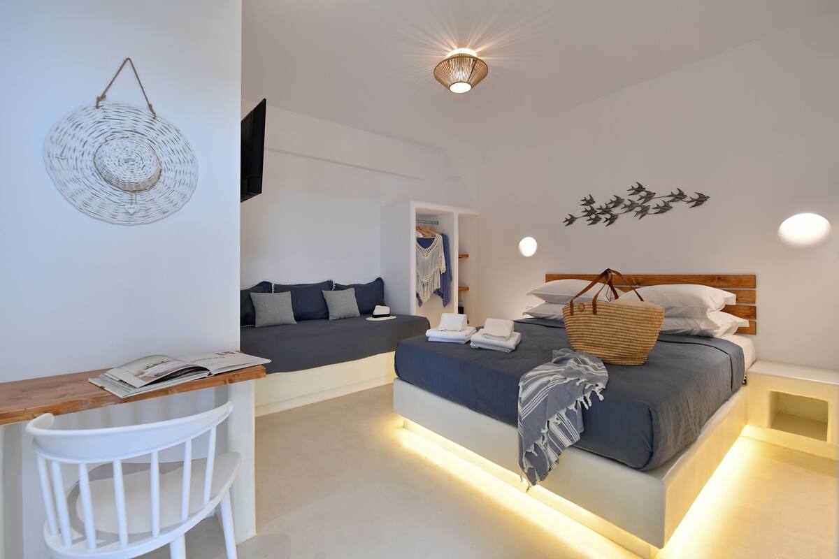 Quarto moderno com cama, mesa de cabeceira e um espaço de estar com almofadas.