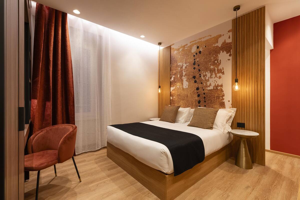 Quarto moderno com cama grande, mesa de cabeceira pequena, uma cadeira e parede com design texturizado.