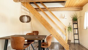 Uma sala de jantar com mesa de madeira e cadeiras de couro, escada de madeira e planta em vaso.