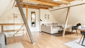 Quarto estilo loft com vigas de madeira aparentes, um sofá branco, uma mesa de jantar e um espelho.