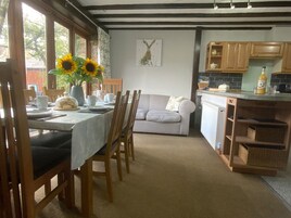Uma sala de jantar com uma mesa posta para quatro pessoas, um sofá riscado, armários de madeira e uma área de cozinha com bancada.