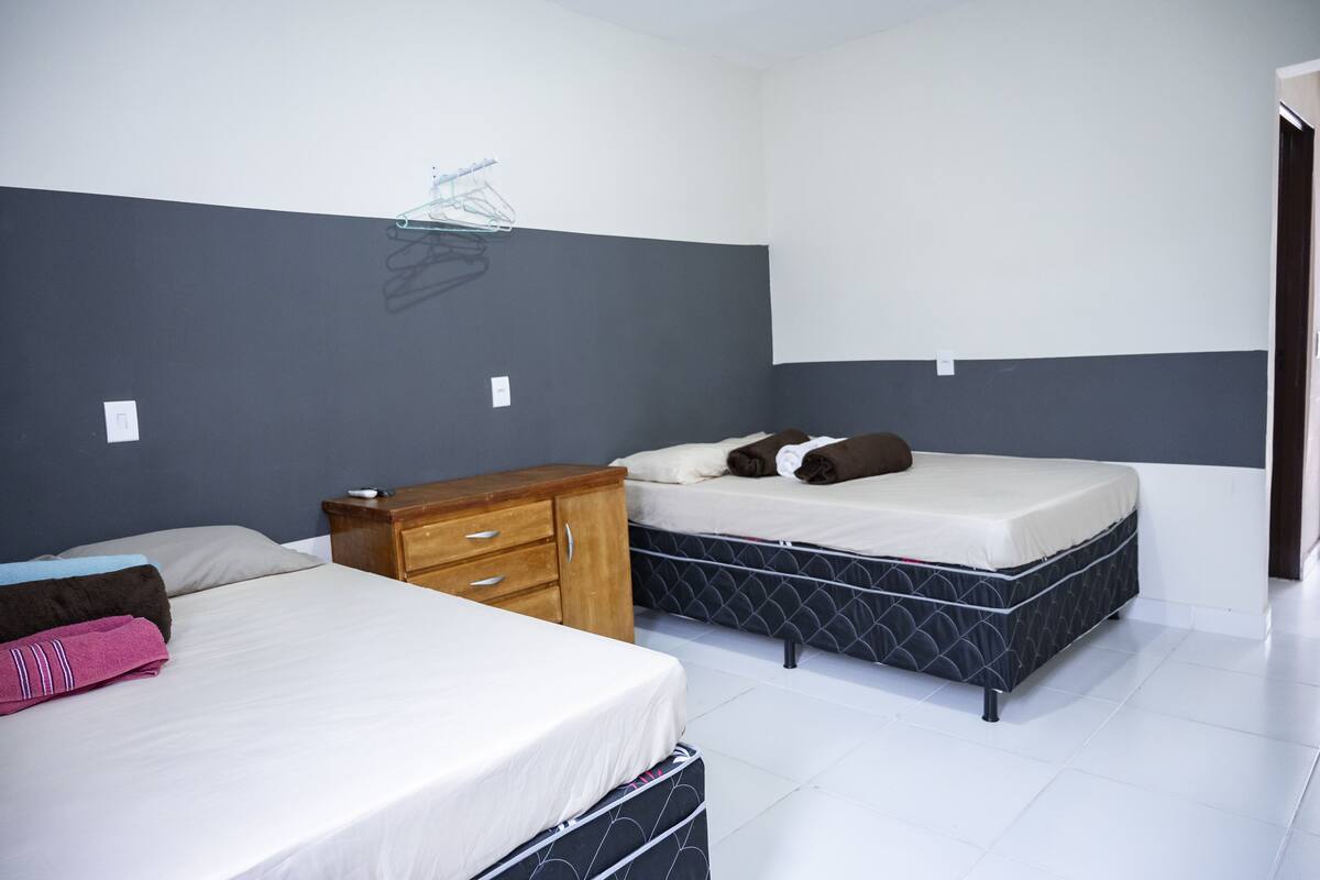 Quarto com duas camas, cômoda de madeira e um varal fixado na parede.
