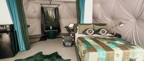 Quarto com cabeceira estofada, edredom acolchoado, tapete verde e pequena mesa de cabeceira com abajur.