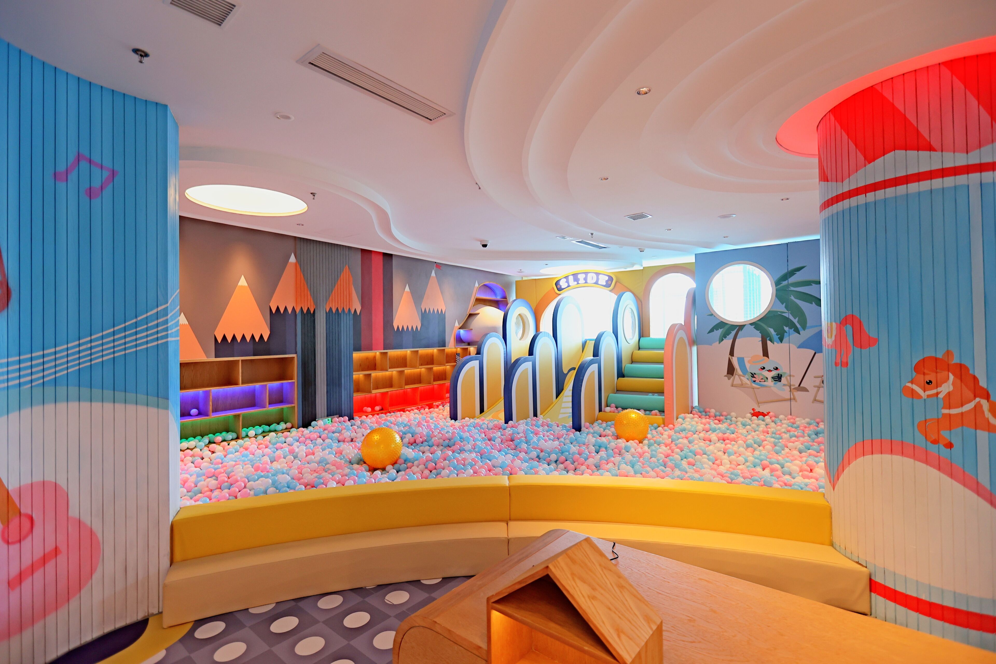 Uma área de recreação infantil com piscinas de bolas coloridas, estruturas de recreação macias e um escorregador.