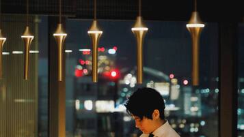 Um bar com vista para a cidade, garrafas de álcool e luminárias penduradas.