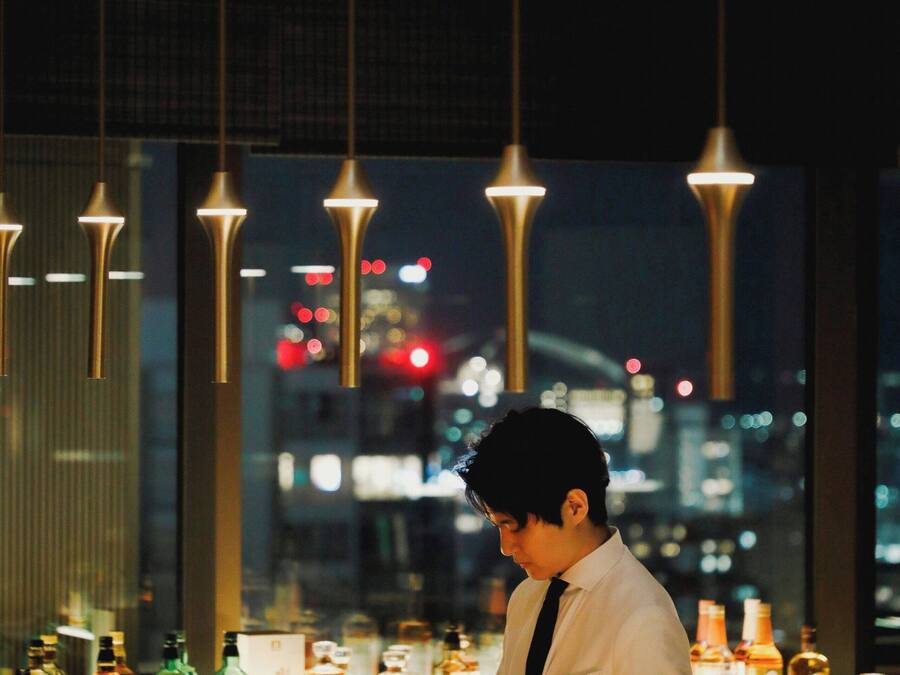 Um bar com vista para a cidade, garrafas de álcool e luminárias penduradas.