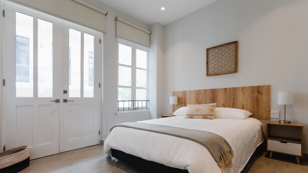Quarto com cama grande, cabeceira de madeira, mesas de cabeceira e janela com persianas.