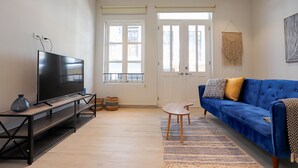 Uma sala de estar moderna com uma TV de tela plana sobre um suporte de madeira, um sofá azul com almofadas e um tapete estampado.