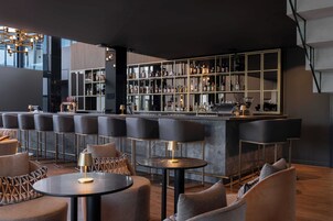 Uma área de bar com design moderno, destacando um balcão, diversas opções de assento e uma variedade de garrafas expostas em prateleiras.