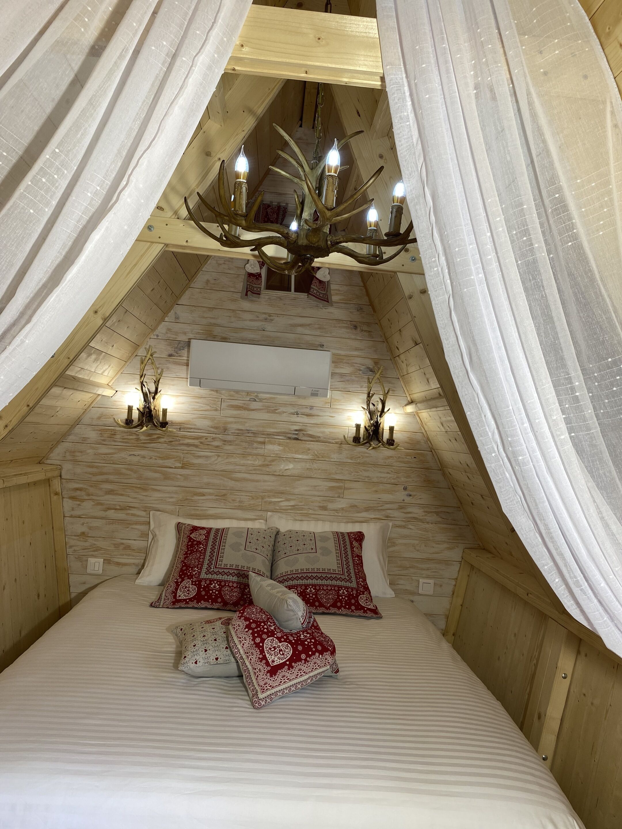 Um quarto de sótão aconchegante, com teto inclinado, paredes de madeira e cama com roupa de cama estampada em vermelho e branco.
