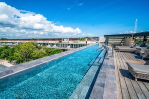 Piscina infinita no terraço, com água azul cristalina, rodeada por cadeiras de descanso e um deck de madeira.