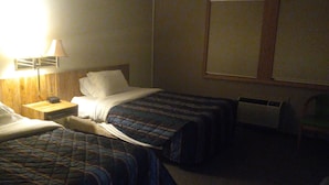 Quarto de hotel com duas camas, uma mesa de cabeceira com abajur e uma janela grande com persianas.