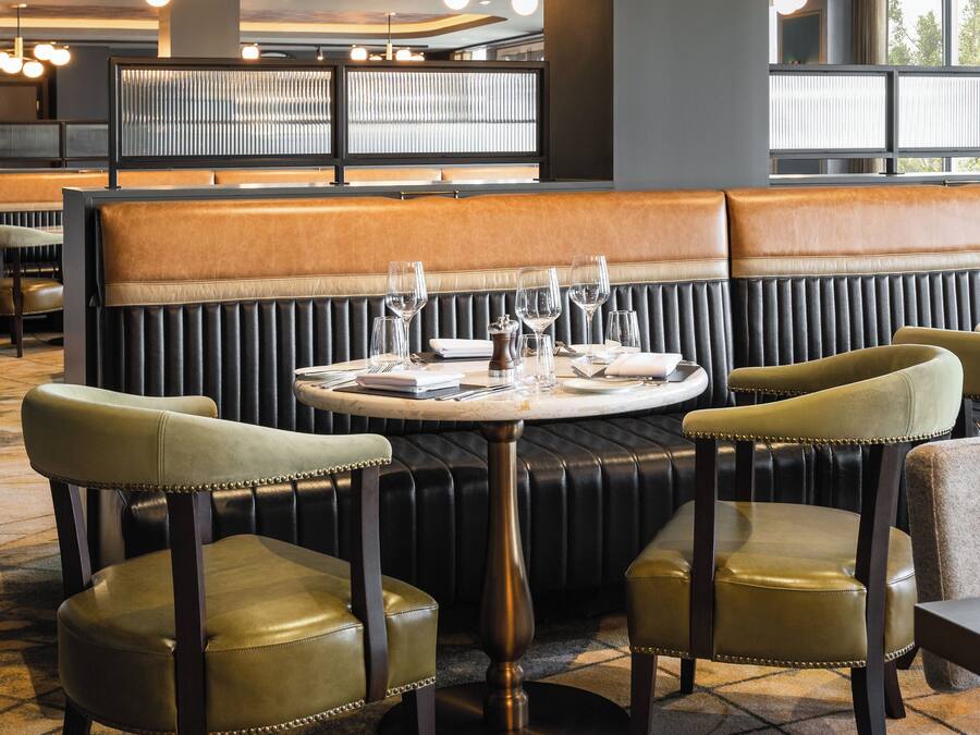 Um restaurante com assentos em cabine, uma mesa redonda com tampo de mármore e piso estampado.