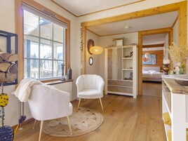 Um quarto acolhedor com uma janela grande, uma cadeira branca, piso de madeira e uma estante rústica.