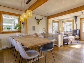 Uma sala de jantar acolhedora com mesa e cadeiras de madeira, uma cozinha com fogão e uma sala de estar com sofá e lareira.