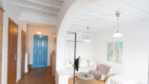 Uma sala de estar ampla com uma porta azul, um sofá branco, uma mesinha redonda e um abajur.