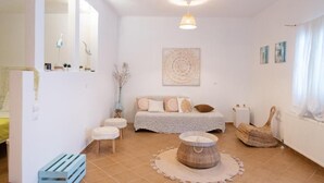 Um quarto claro e arejado, com uma cama, uma mesa de madeira redonda e uma cadeira de fibra natural.