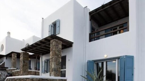 Um edifício branco com pilares de pedra, persianas azuis e um pátio com calçada de pedra.