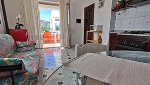 Sala de estar com sofá, mesa de jantar com cadeiras, cozinha com fogão e vista para o exterior.