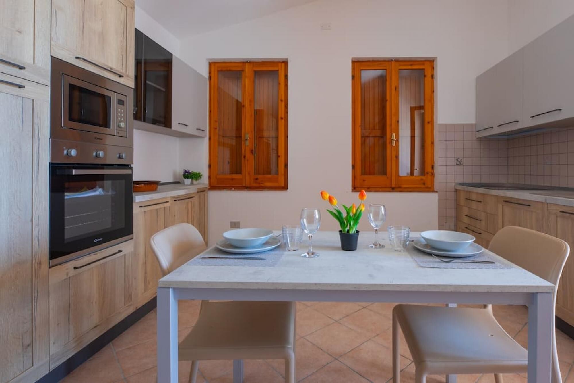 Uma cozinha moderna com armários de madeira, forno embutido e uma mesa de jantar posta para dois, com cadeiras.