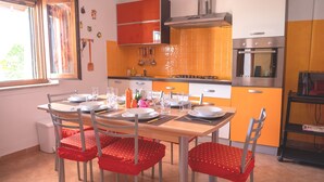 Cozinha moderna com armários laranja, forno de aço inoxidável e área de jantar para quatro com cadeiras vermelhas.