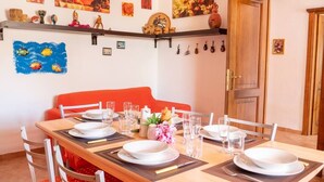 Uma sala de jantar com uma mesa de madeira posta para quatro pessoas, rodeada por cadeiras vermelhas com bolinhas brancas.