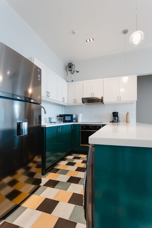 Cozinha moderna com geladeira de aço inoxidável, armários brancos, uma ilha verde-água e piso estampado.