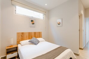 Quarto moderno com cabeceira de madeira, colcha branca, manta estampada e duas obras de arte emolduradas na parede.