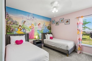 Quarto com duas camas, um mural, quadros emoldurados e uma janela com cortinas.